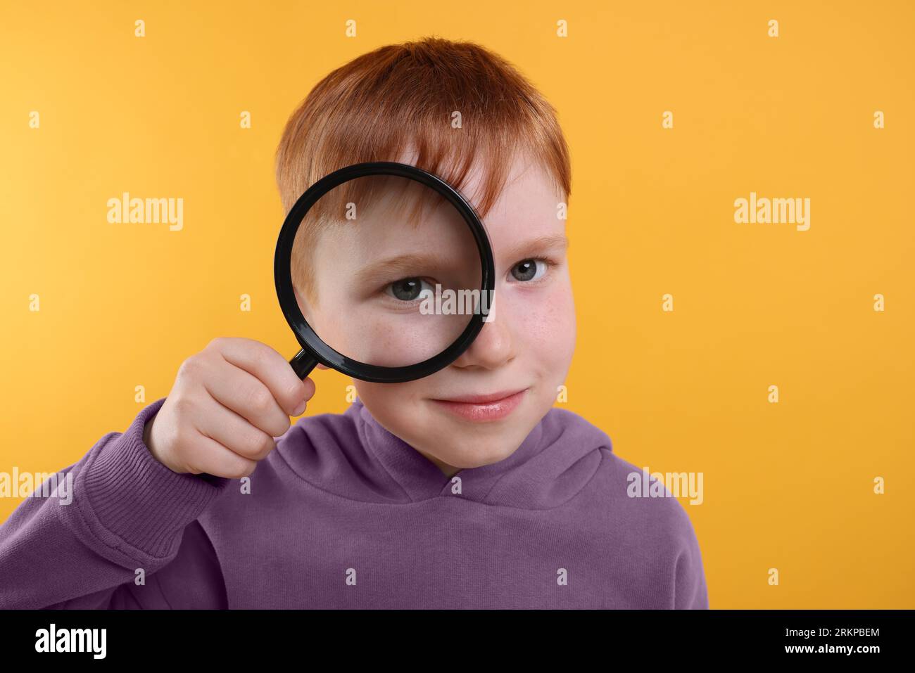 Boy looking through magnifier glass on yellow background Stock Photo ...