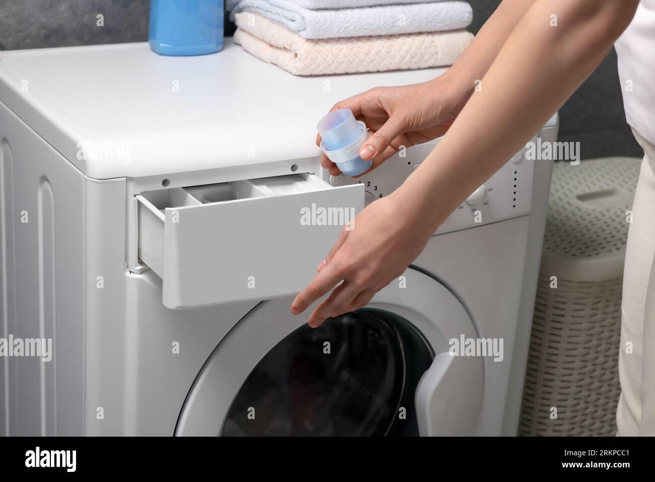 Woman pouring fabric softener from cap into washing machine, closeup ...