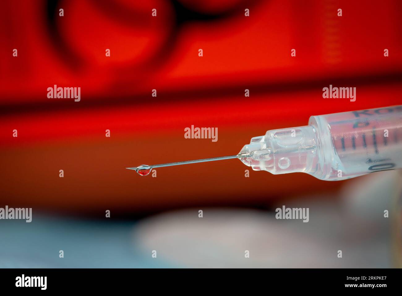 Syringe hypodermic needle, at tip is a small drop, inside a biohazard ...