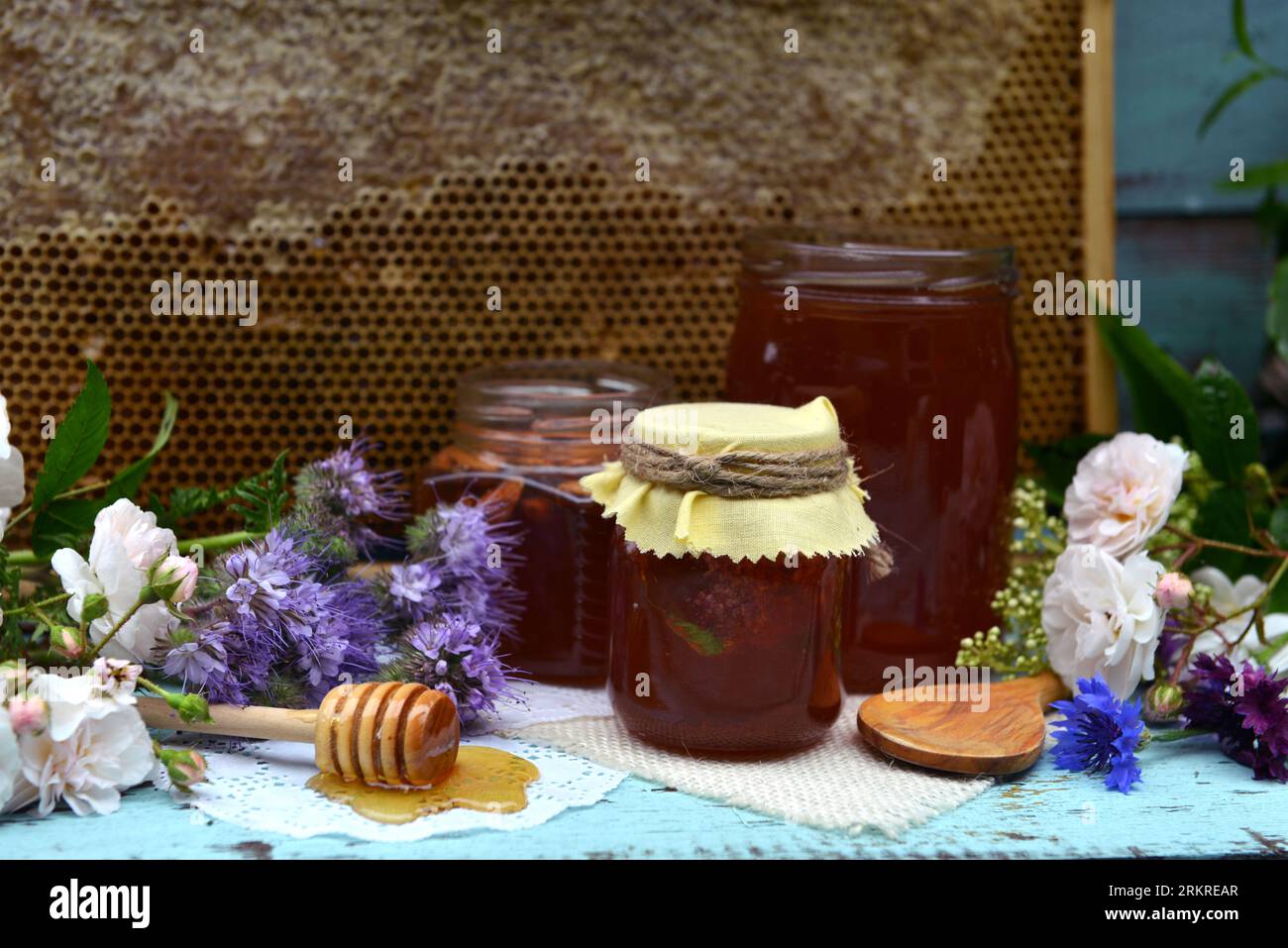 Still life with natural honey in jar, dipper, flowers and stick against ...