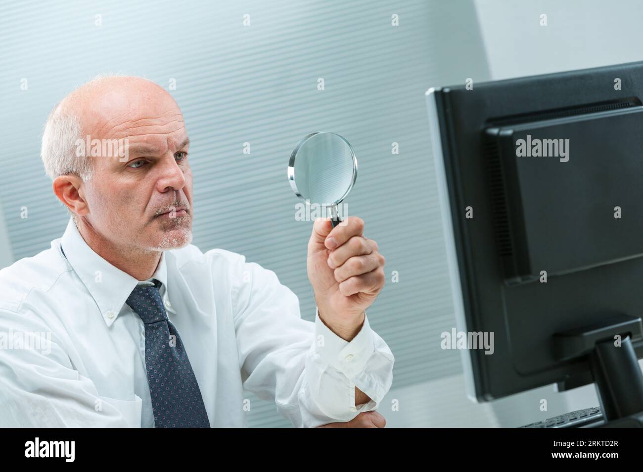 Older businessman in white shirt and tie scrutinizes a computer screen ...