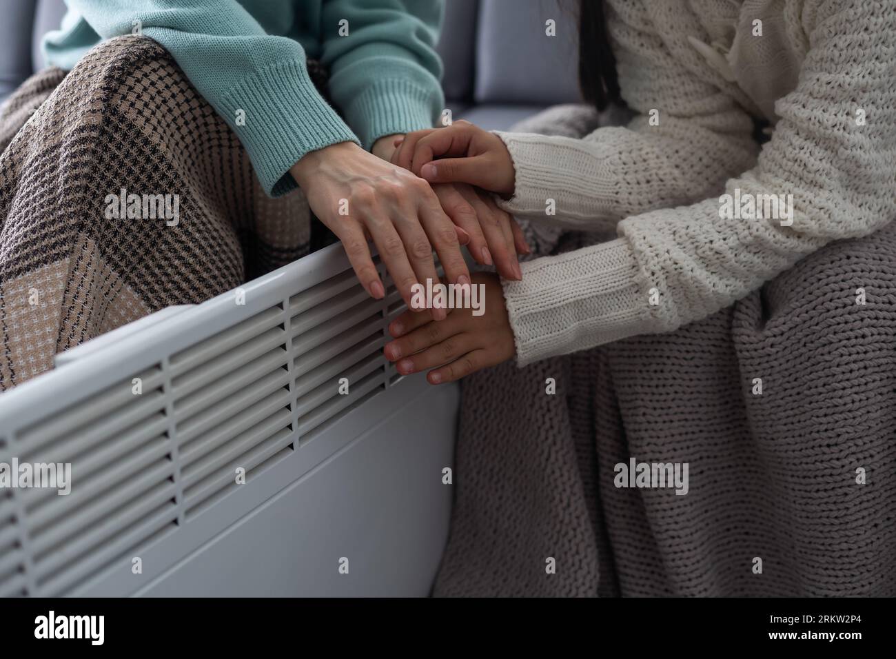 Mother and child warming hands near electric heater at home, closeup ...