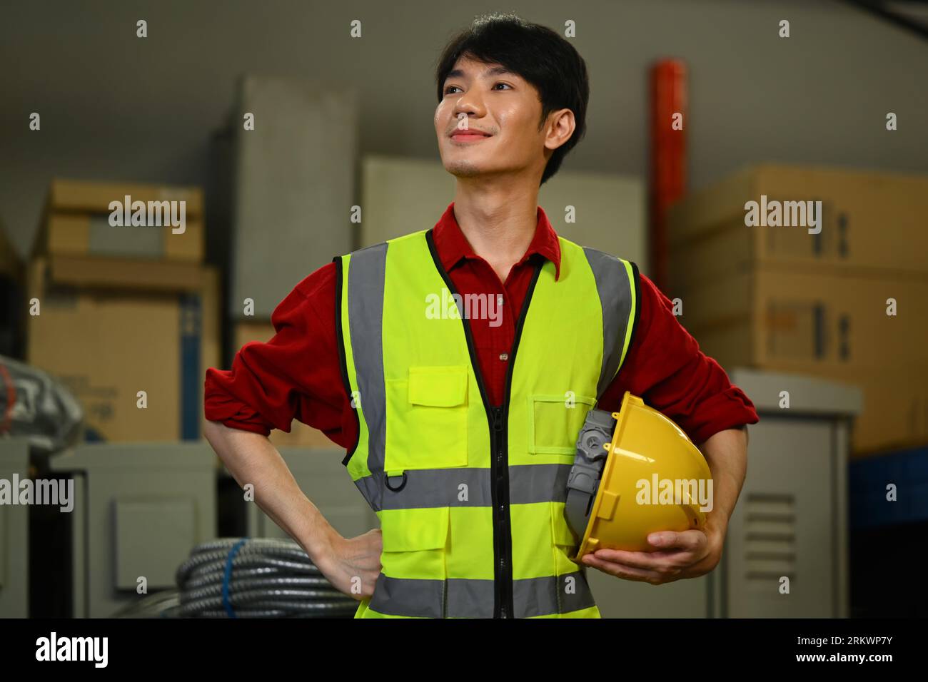 Handsome warehouse worker wearing security vest standing near the stack ...