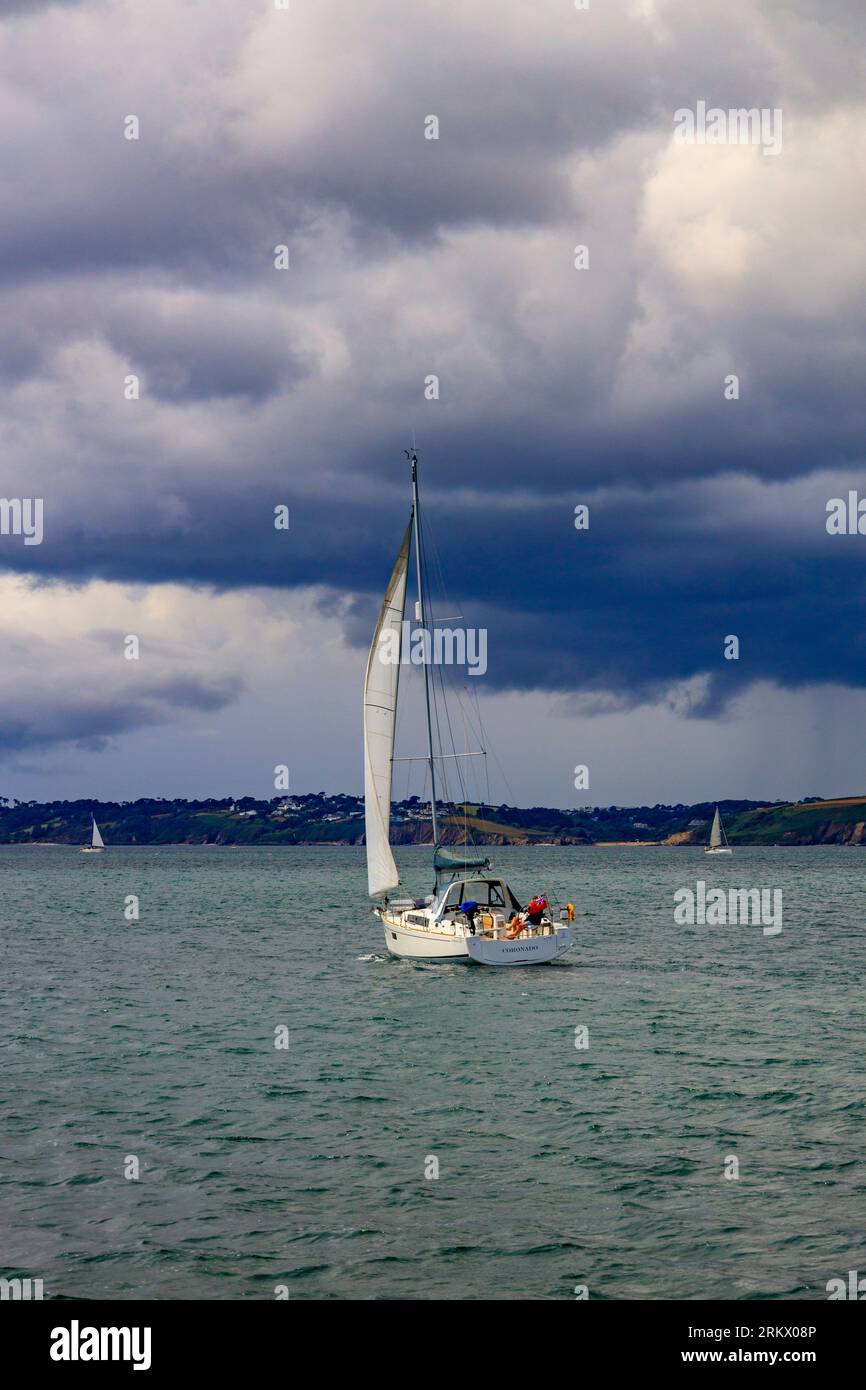 A yacht makes its way down the River Fal out of Falmouth under dark ...