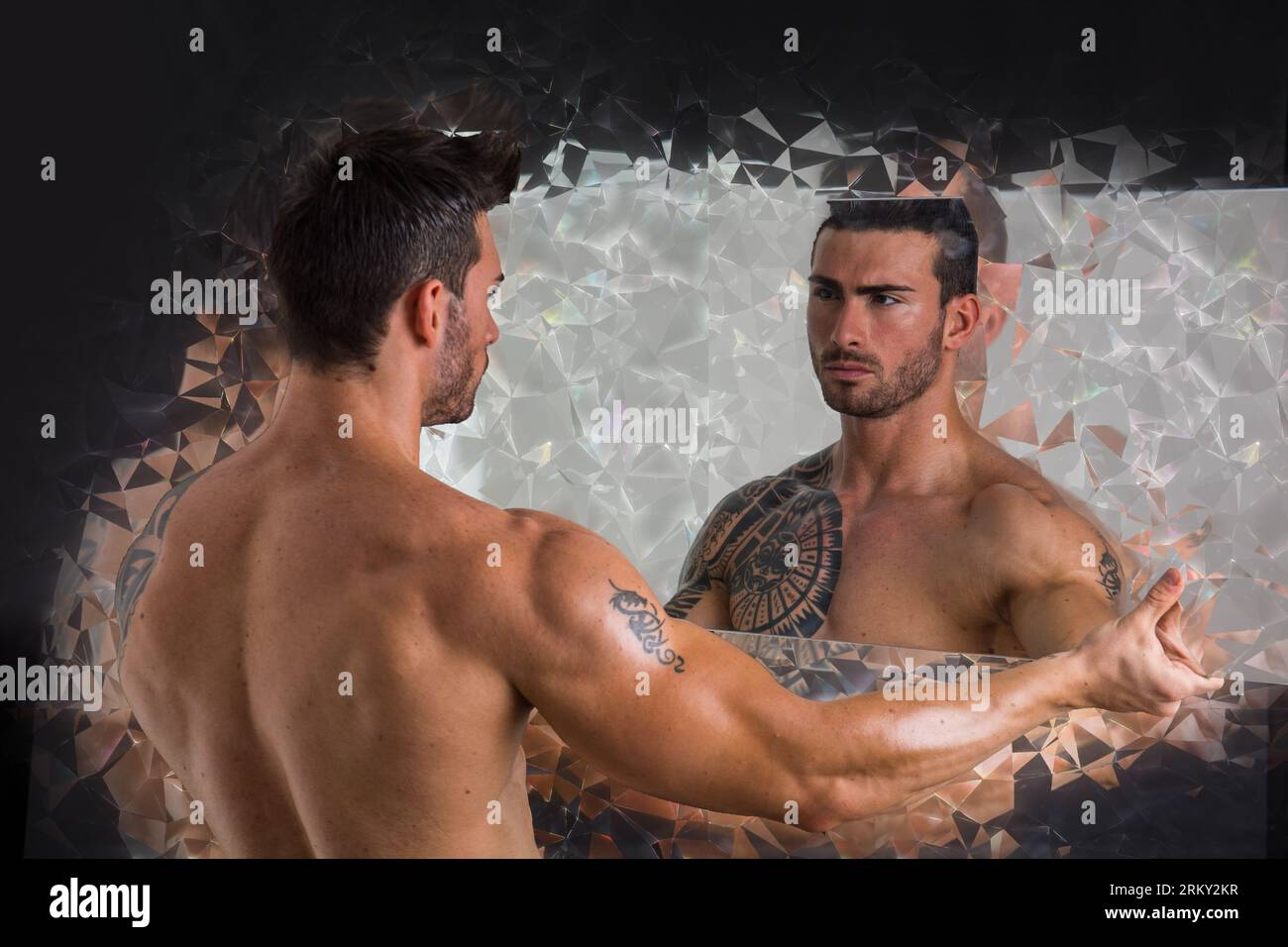 A muscular man standing by a mirror, looking at his own reflection ...