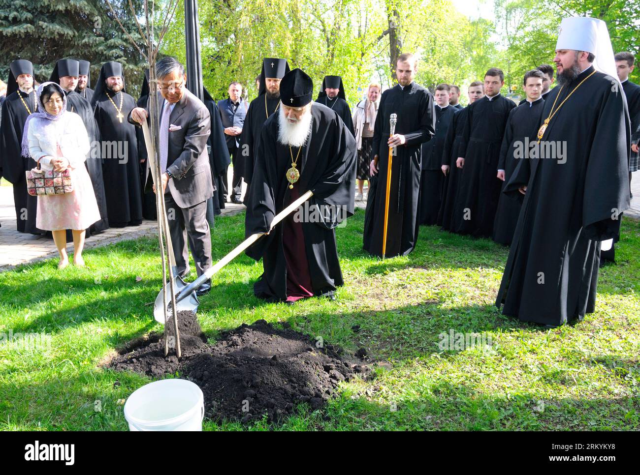 Old Orthodox priest planting tree with shovel in a church garden, monks ...