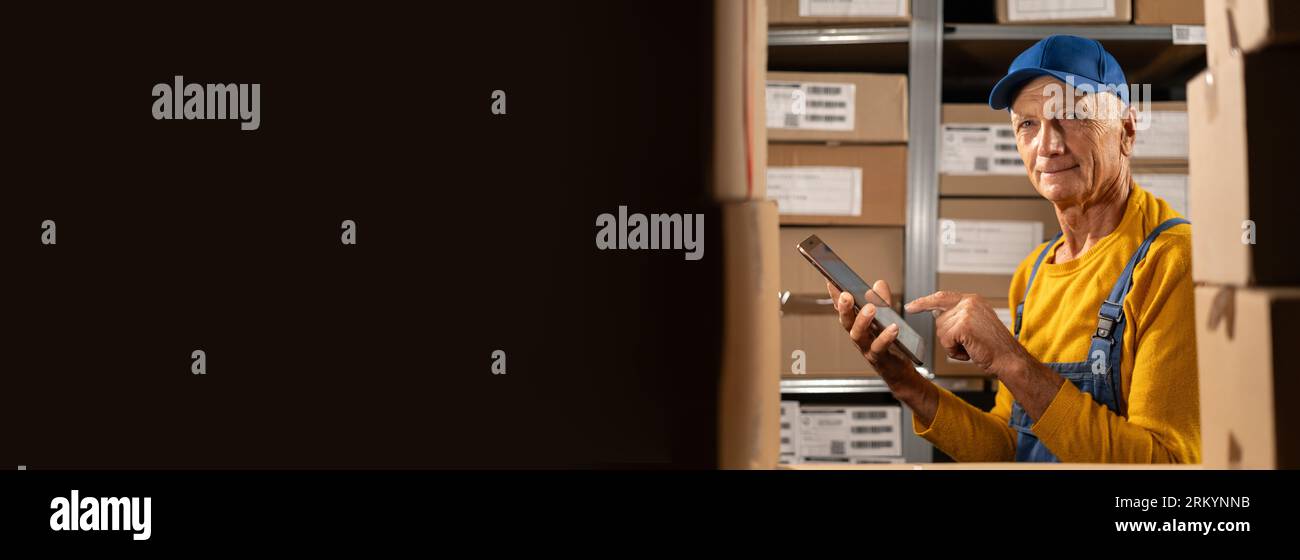 Elderly warehouse inventory manager uses digital tablet to check stock ...