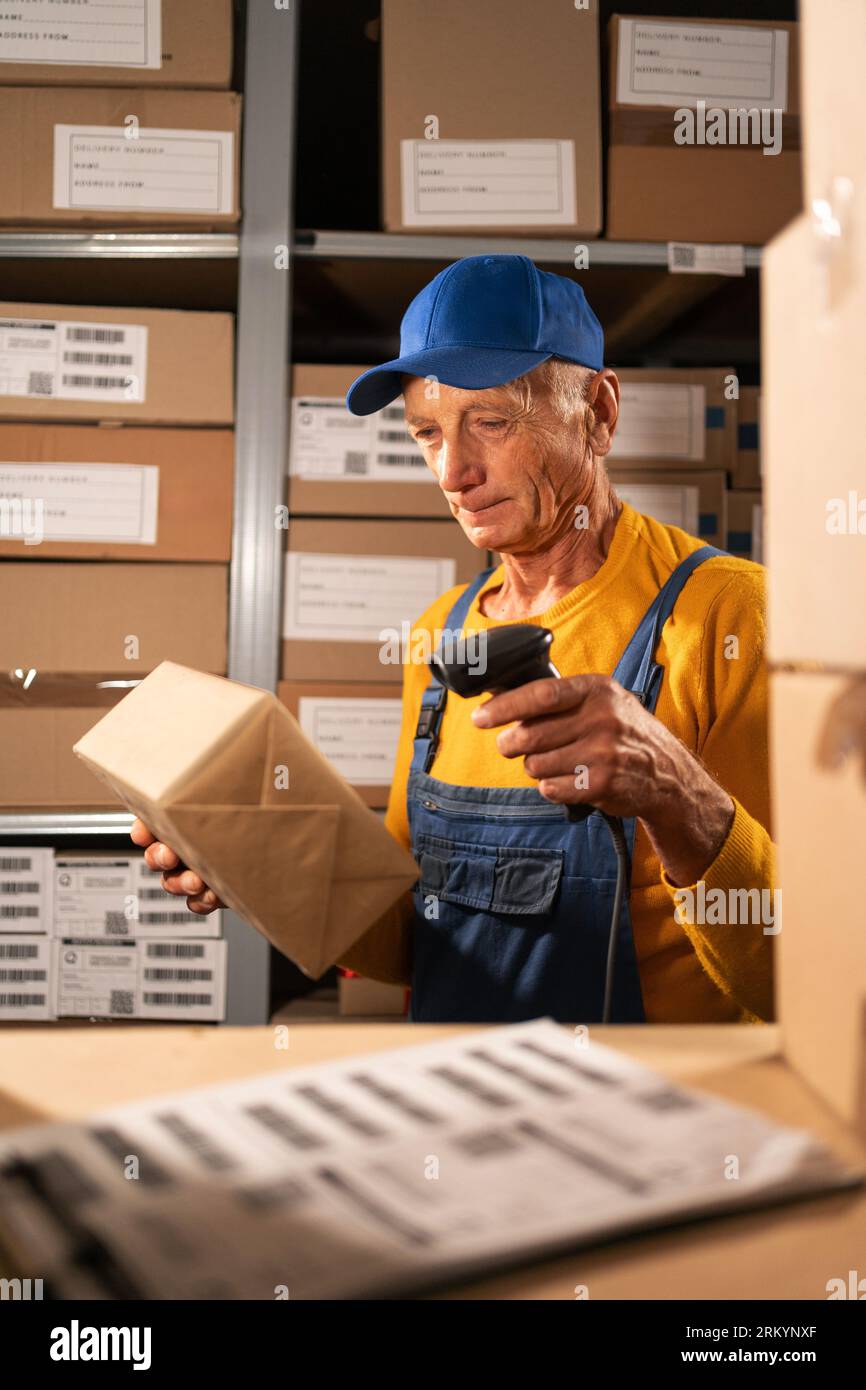 Old male warehouse worker scans cardboard box with Barcode Scanner ...