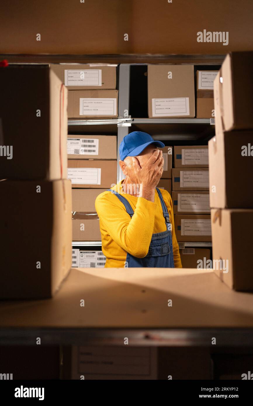 Tired, exhausted warehouse elderly worker has problems with inventory ...