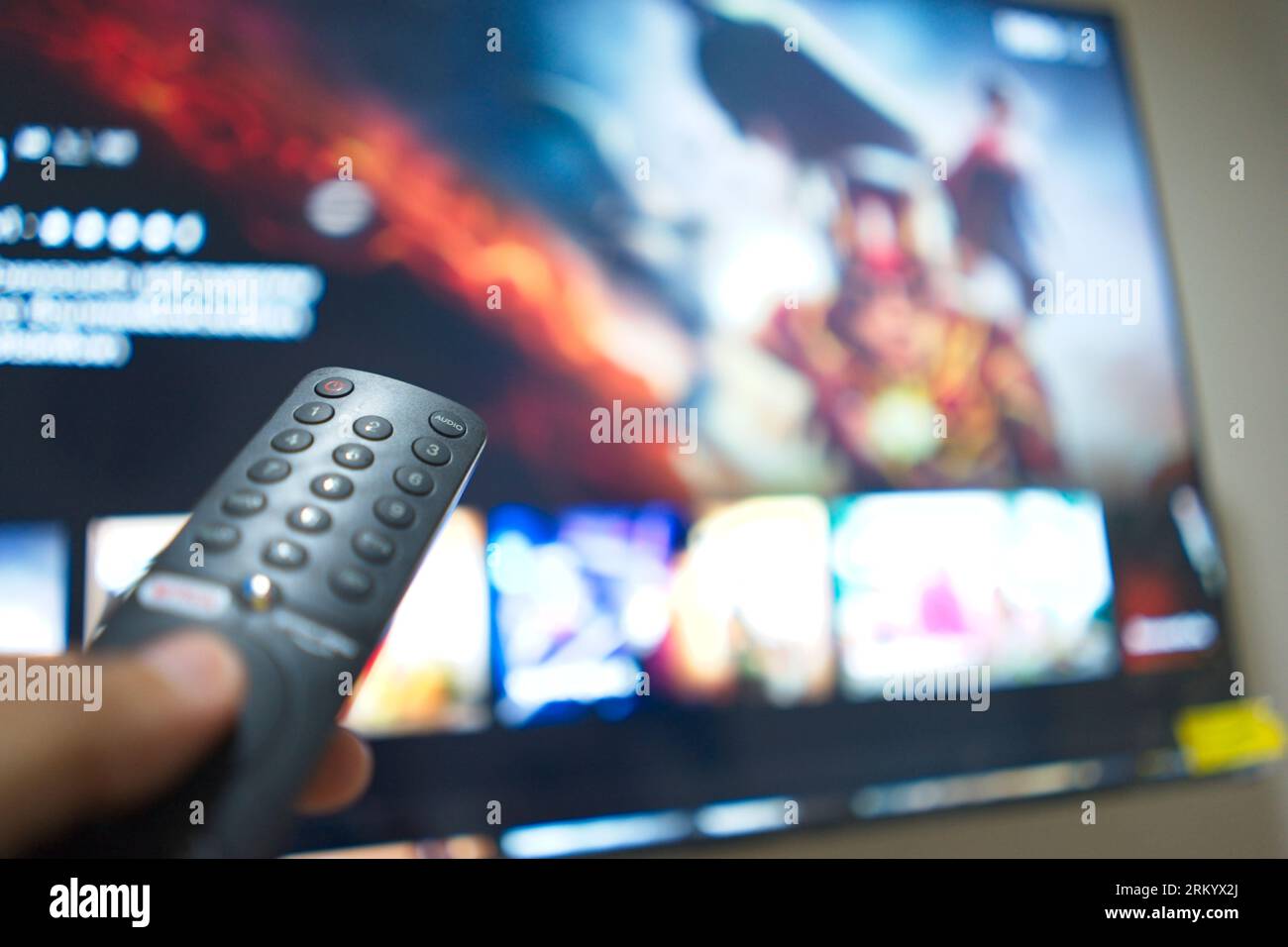 Hand with TV remote control, switching TV series from streaming service ...