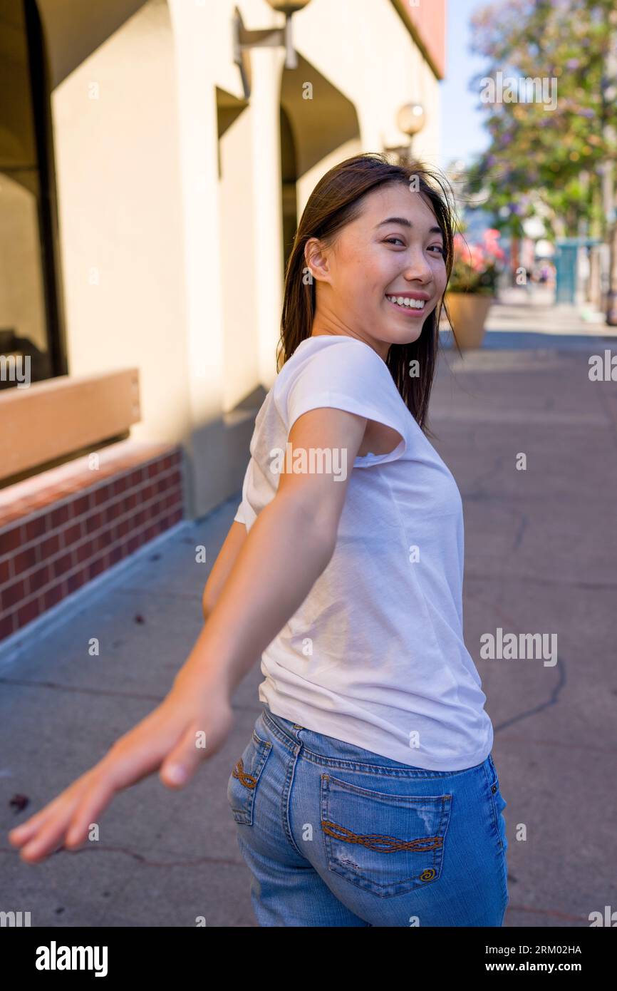 Young Asian Woman Looking Back and Reaching Hand Out to Hold | Downtown Sidewalk Stock Photo - Alamy