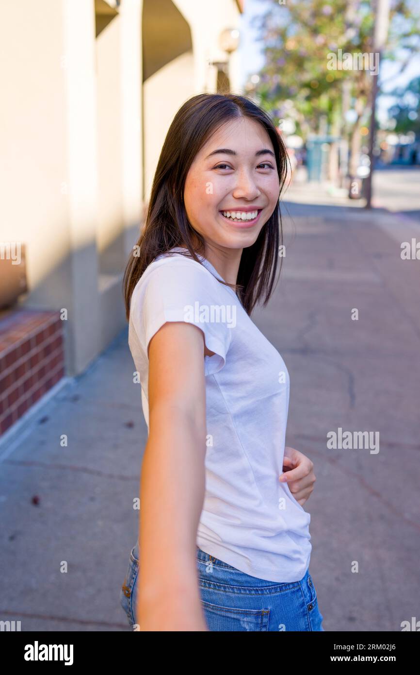 Young Asian Woman Looking Back and Reaching Hand Out to Hold | Downtown Sidewalk Stock Photo - Alamy