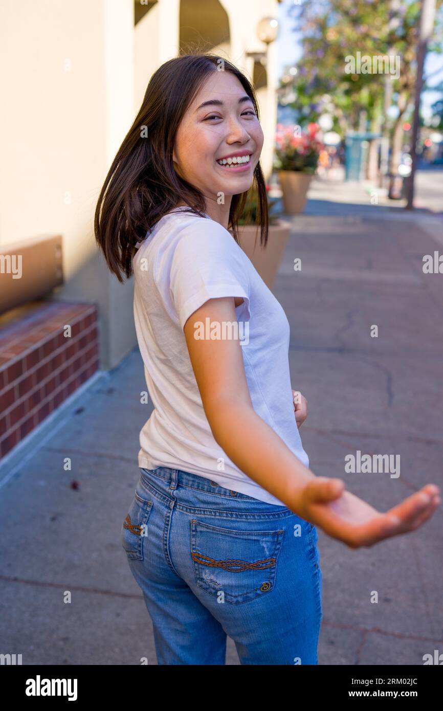 Young Asian Woman Looking Back and Reaching Hand Out to Hold | Downtown Sidewalk Stock Photo - Alamy