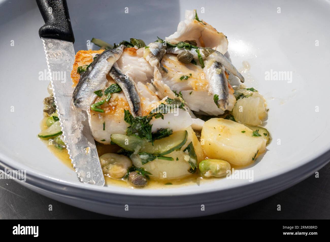 prepared dish of pan fried cod with whitebait capers courgette and ...