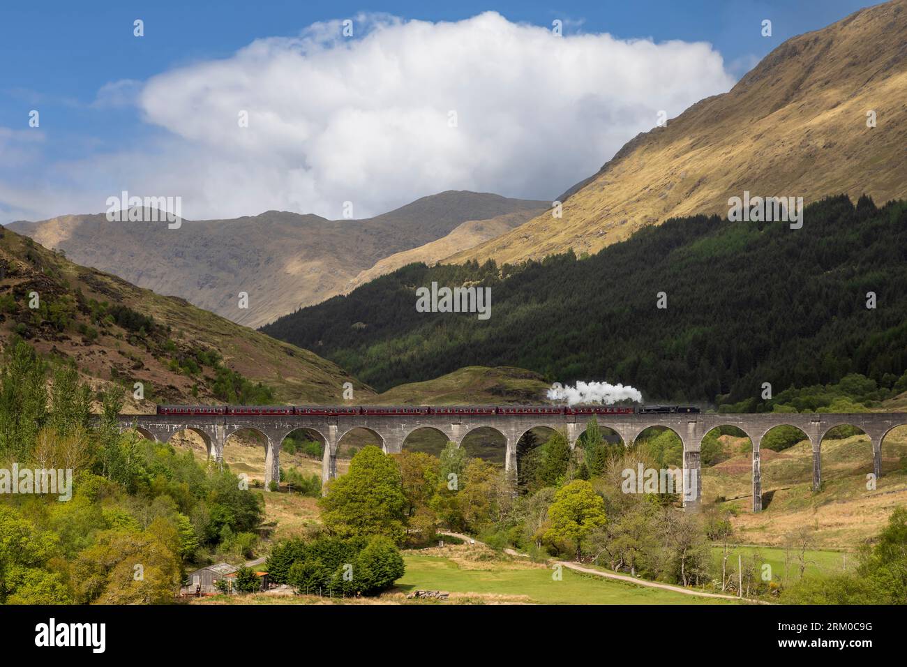 the jacobite steam train crossing glenfinnan viaduct on a sunny day as ...