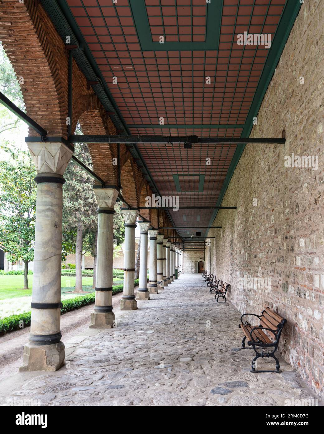 Long covered paved walkway with columns and benches. The walkway is ...