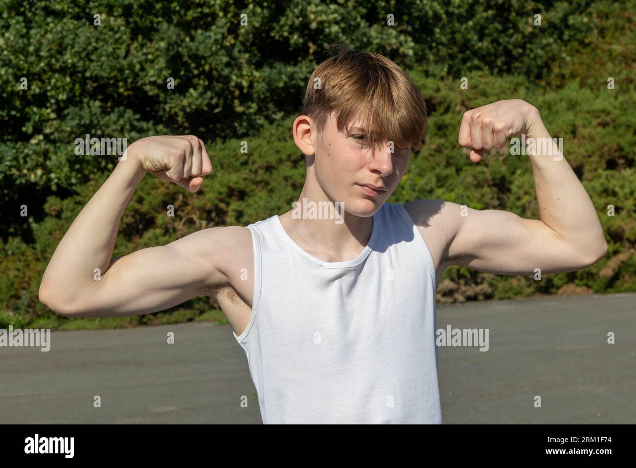 Fit and sporty teenage boy flexing both his biceps Stock Photo - Alamy
