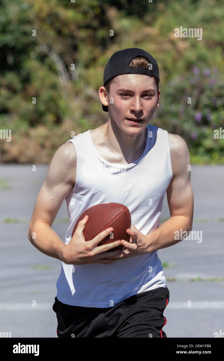 Fit and active teenage boy running outside with an American Football ...