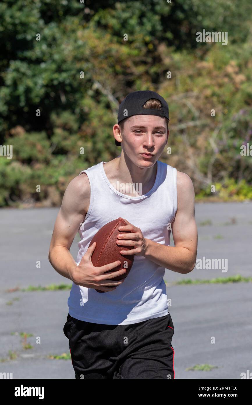 Fit and active teenage boy running outside with an American Football ...