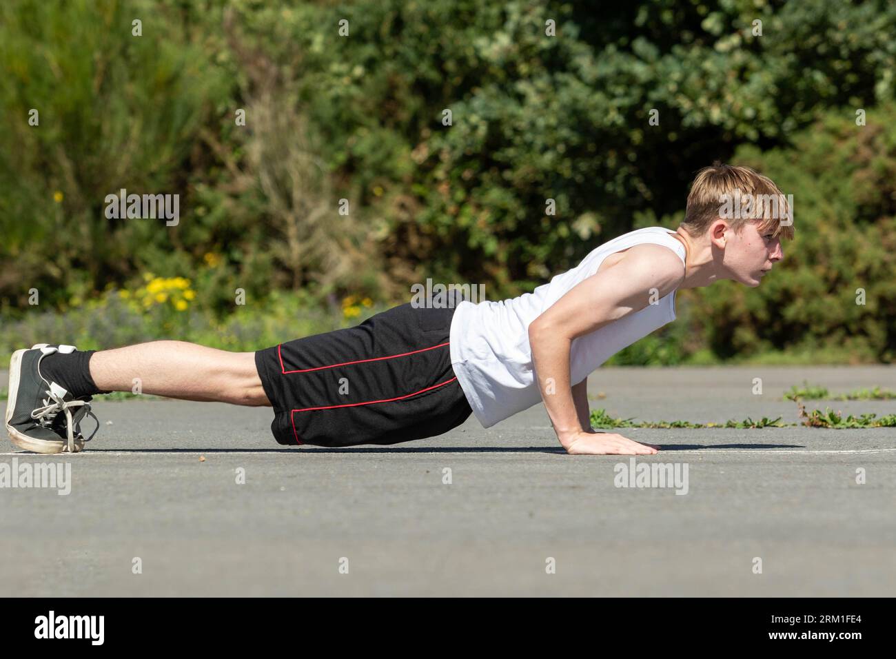 Fit and sporty teenage boy doing press ups outside on a warm summer's ...