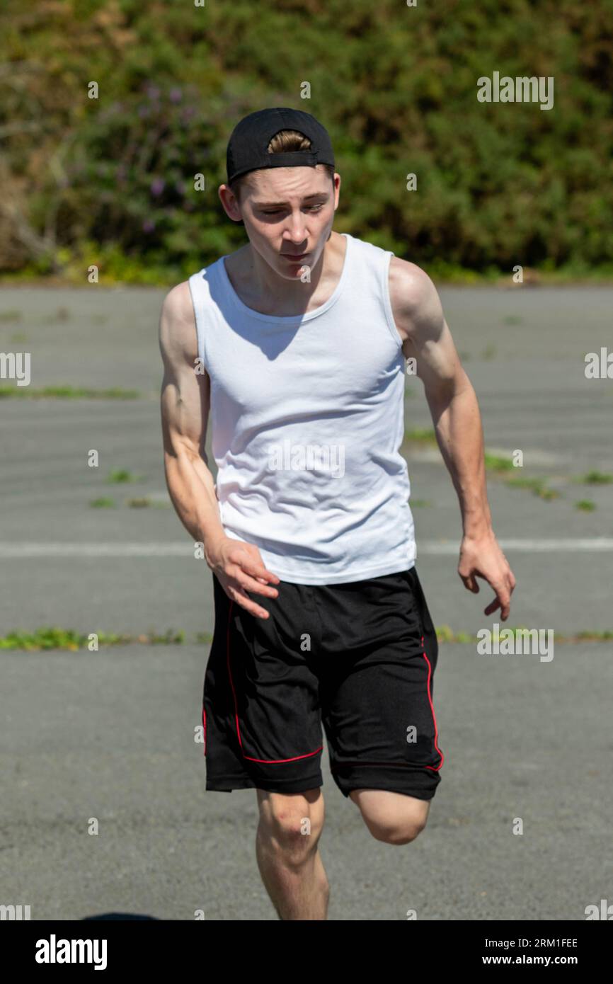 Fit and sporty teenage boy wearing a backwards cap, running outsid eon ...