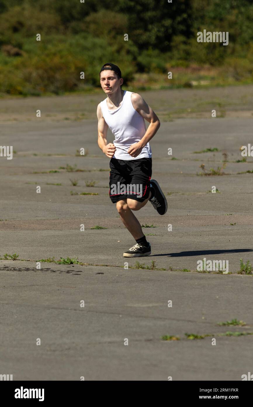 Fit and sporty teenage boy wearing a backwards cap, running outsid eon ...