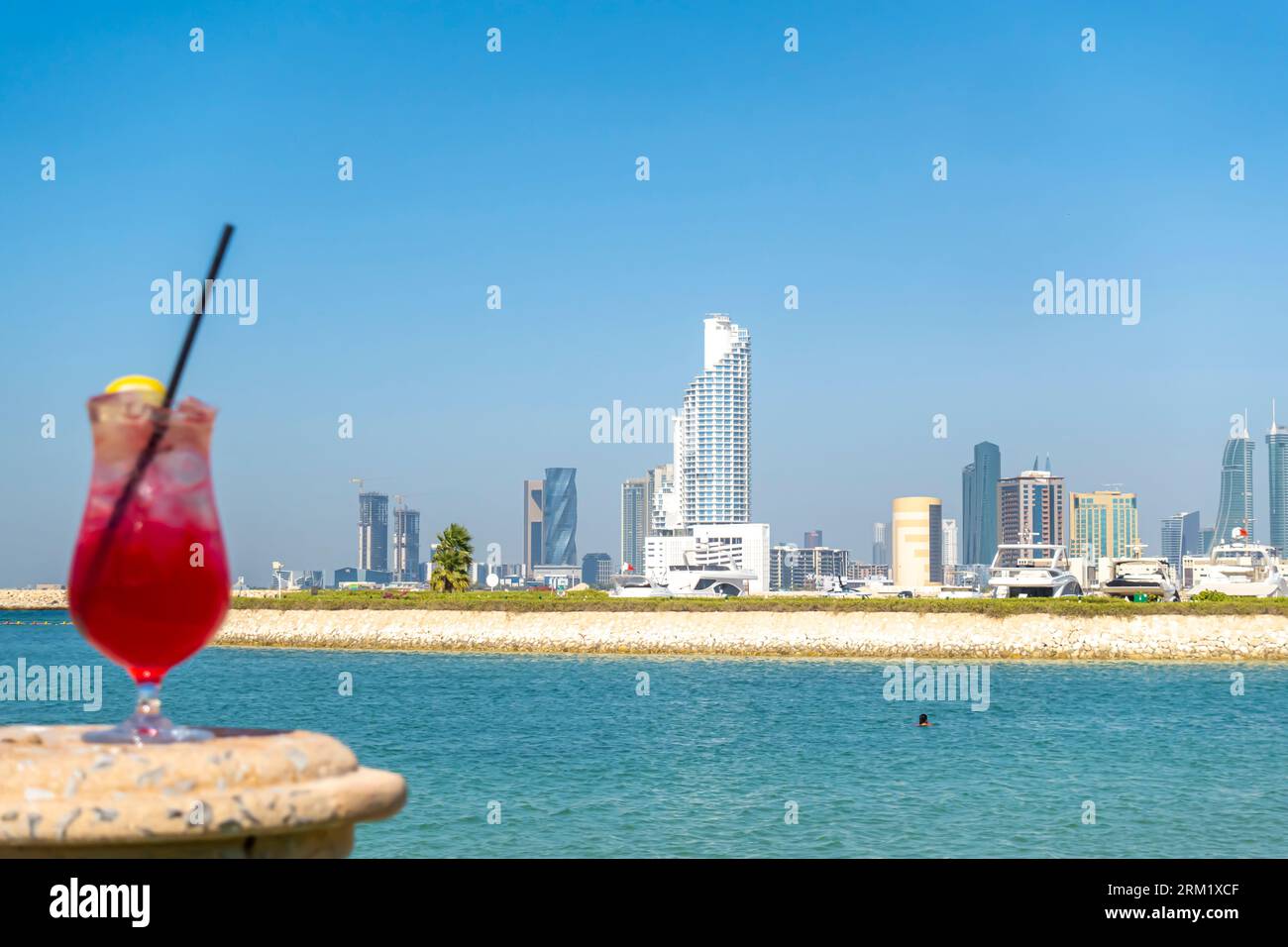 Glass of red drink, lemonade with lemon and straw against Bahrain Bay ...