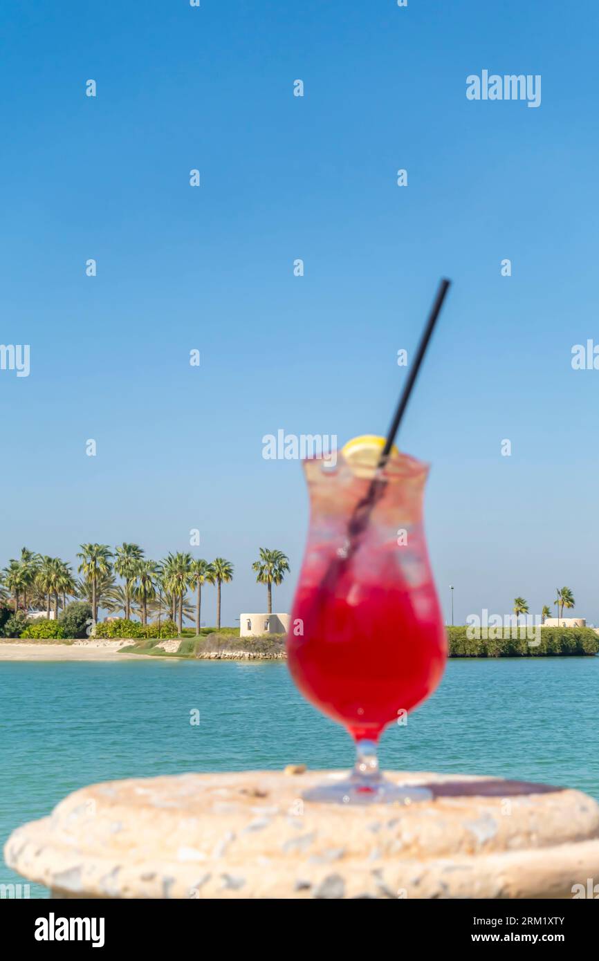 Glass of red drink, lemonade with lemon and straw against Bahrain Bay ...