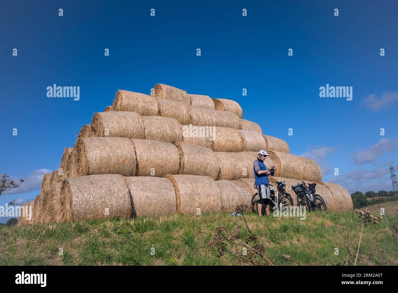 A man takes a rest from bikepacking by a large stack of hay at the edge ...
