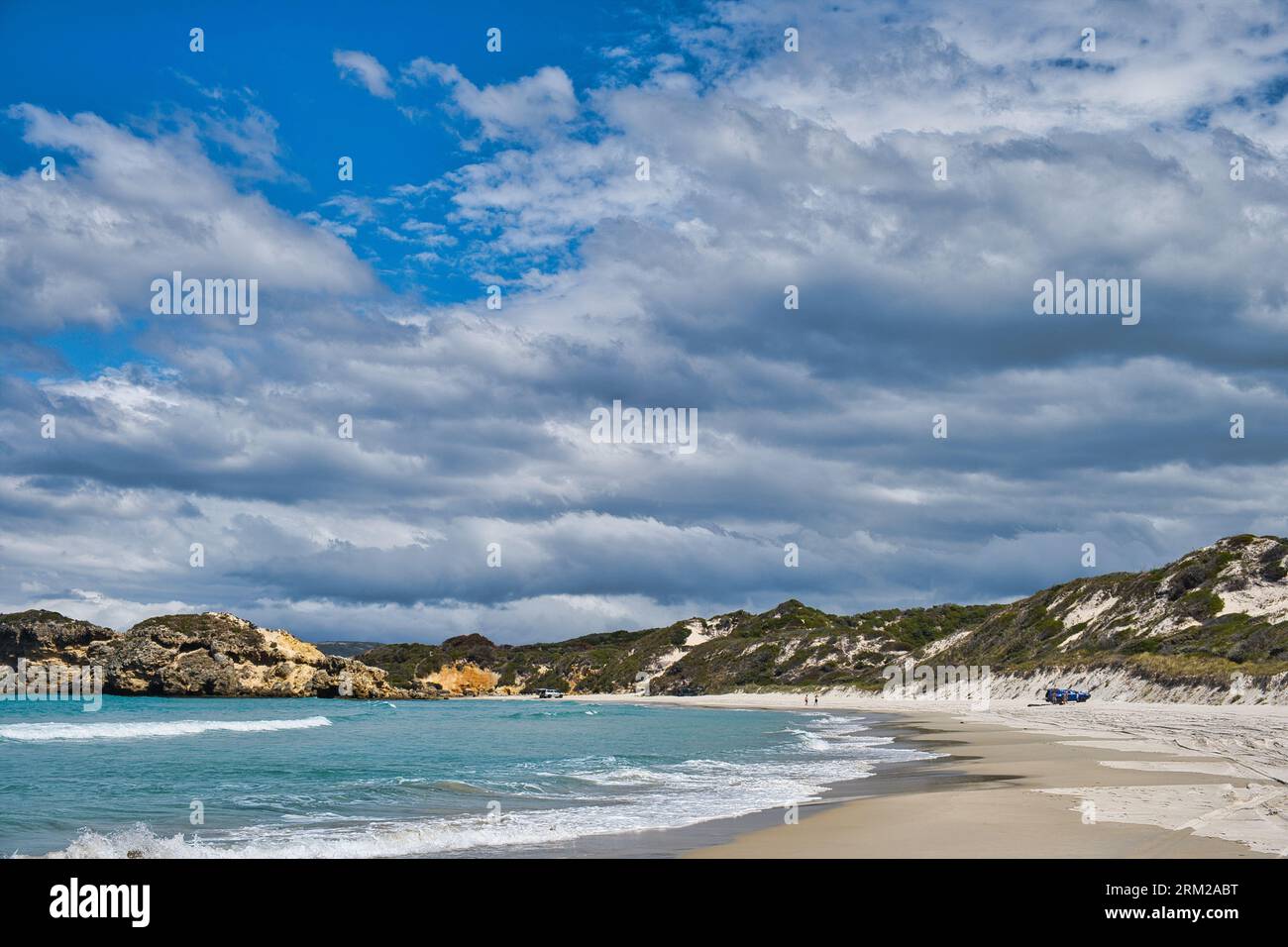 Quiet beach on a bay, with dunes and eroded rocks, under a sky with ...