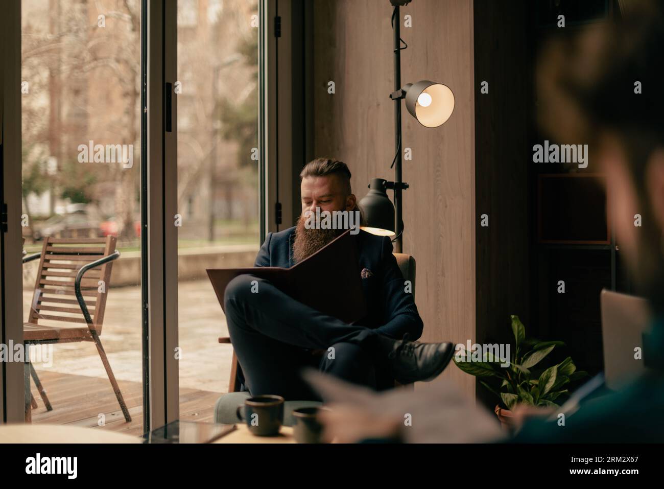 Handsome bearded man writing something on his notepad with his legs ...