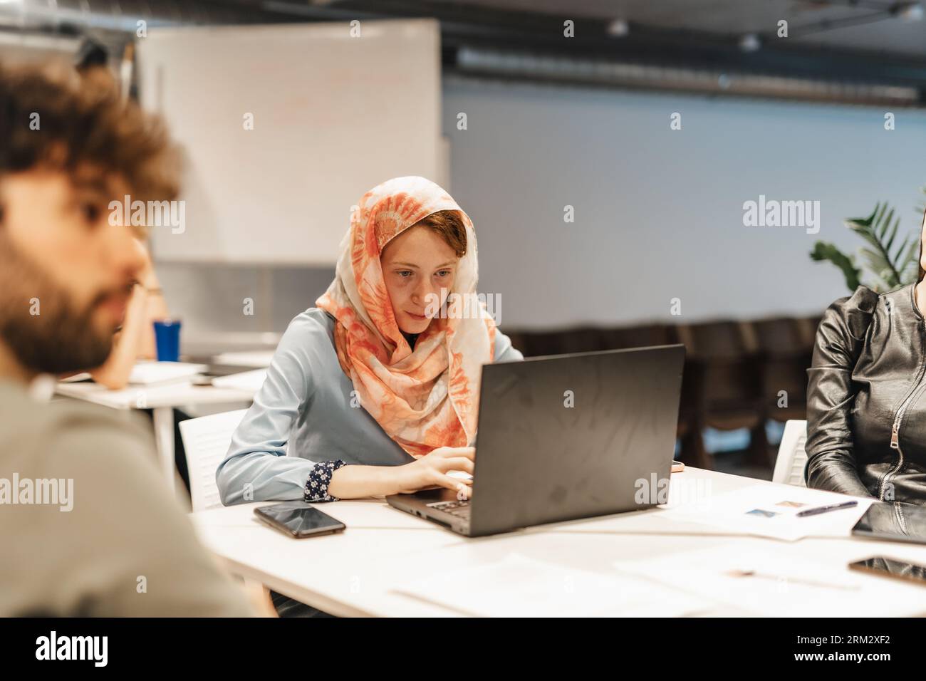 Gorgeous, ginger woman in hijab working on lap top, solving daily tasks ...