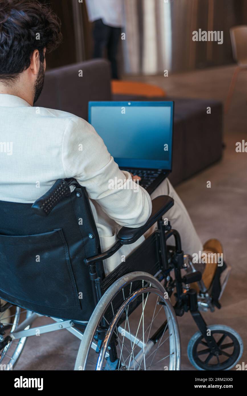 Disabled employee in wheelchair working on lap top. Back view shot ...