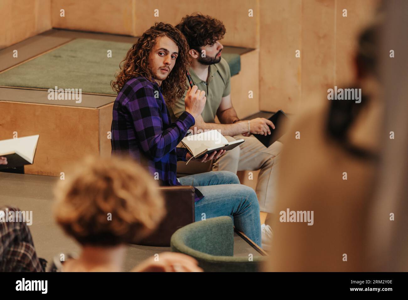 Young faculty student looking back and writing in his notebook at the ...
