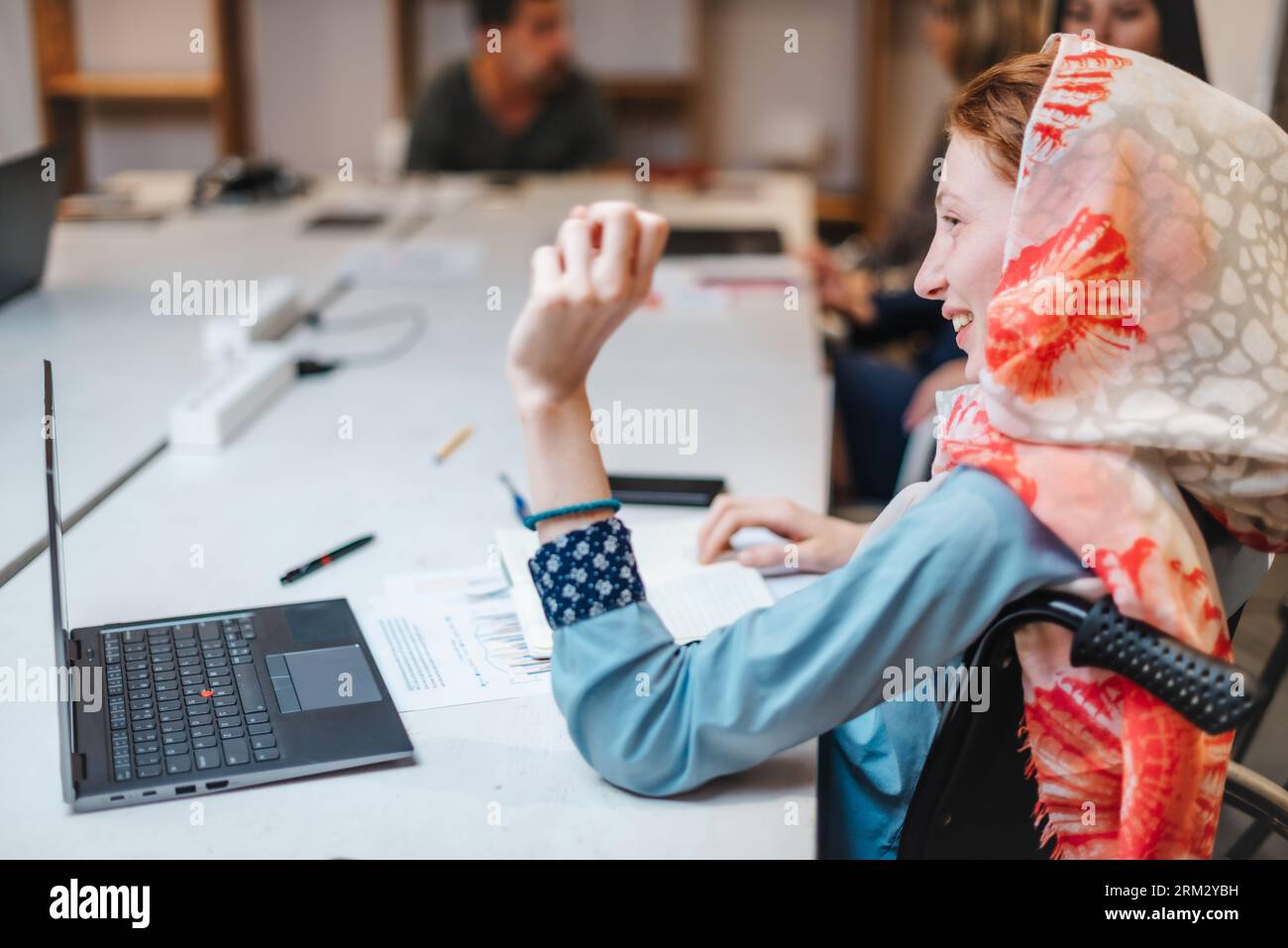 Smiley woman wearing hijab, in wheelchair, discussing with her coworker ...