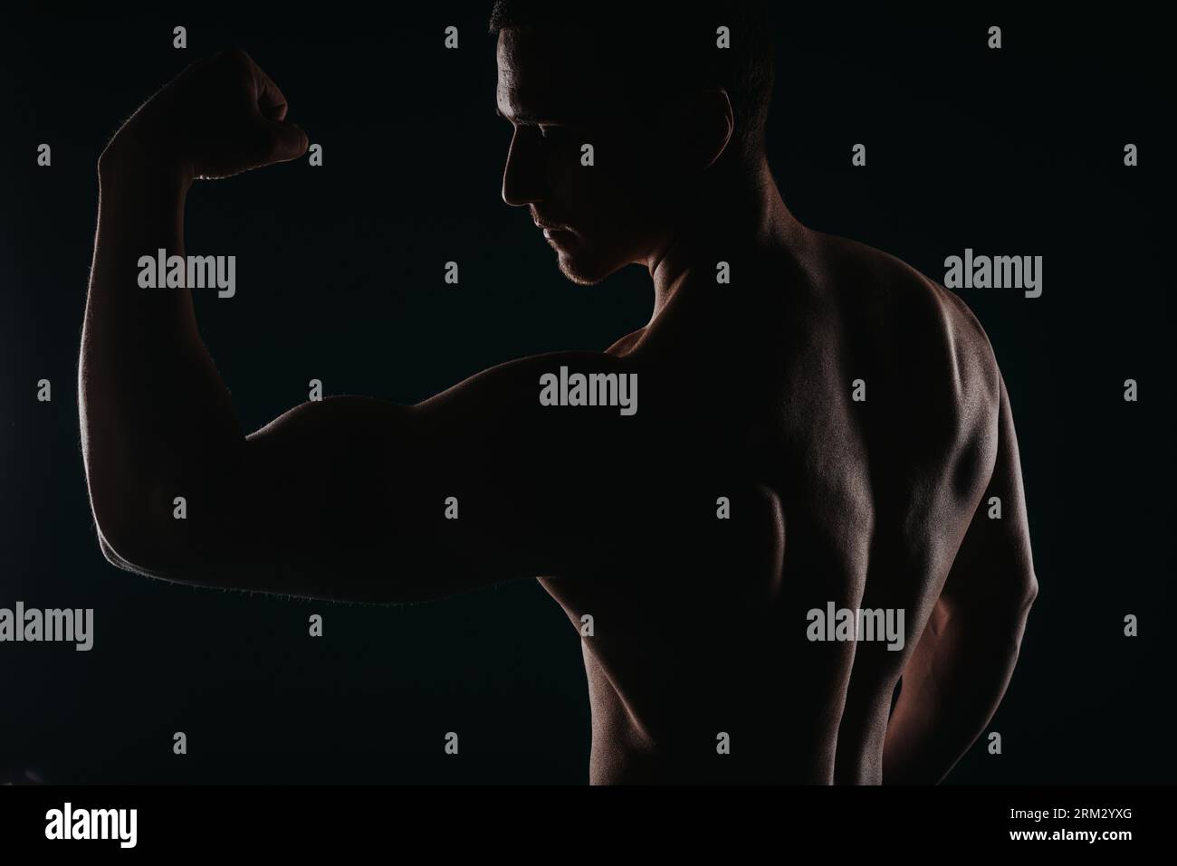 Man showing his back and left arm biceps posing on a dark background ...