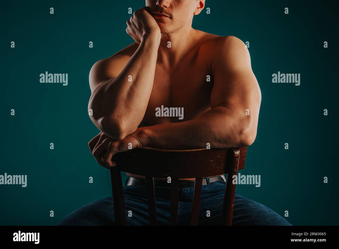 Partial shot of fit bodybuilder sitting on chair and posing for the ...