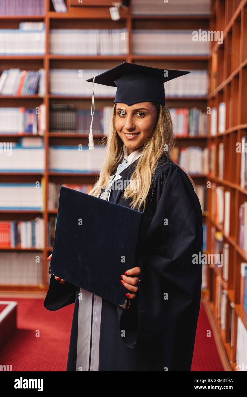 Young and smiling graduate holding her bachelor's degree and wearing a ...