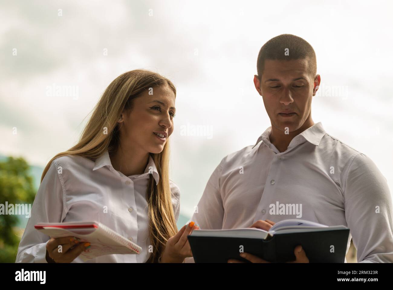 Two well-dressed and young students standing outside with notebooks in ...