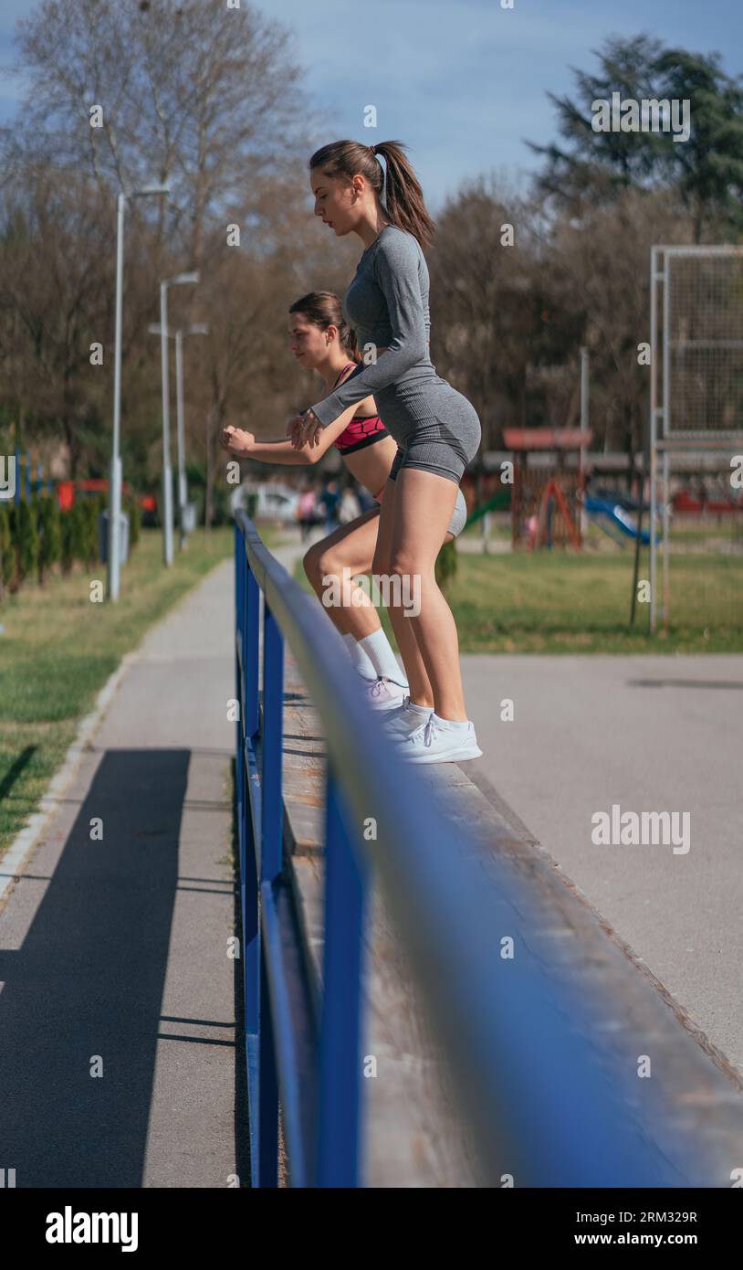 Fit sportsgirls doing jumps on the bench in the park. Side view shot ...