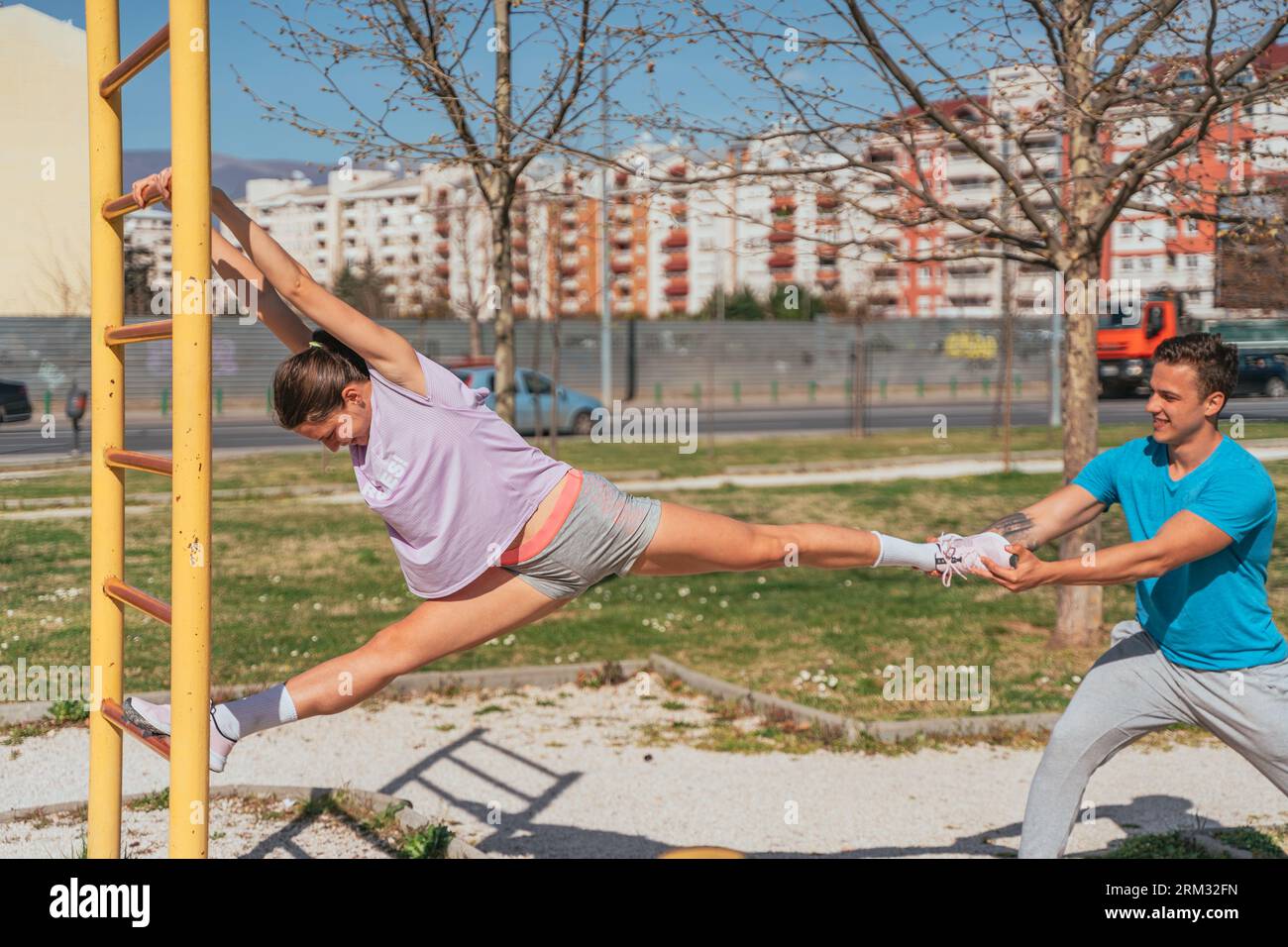 Good looking male person helping his female friend stretching her legs ...