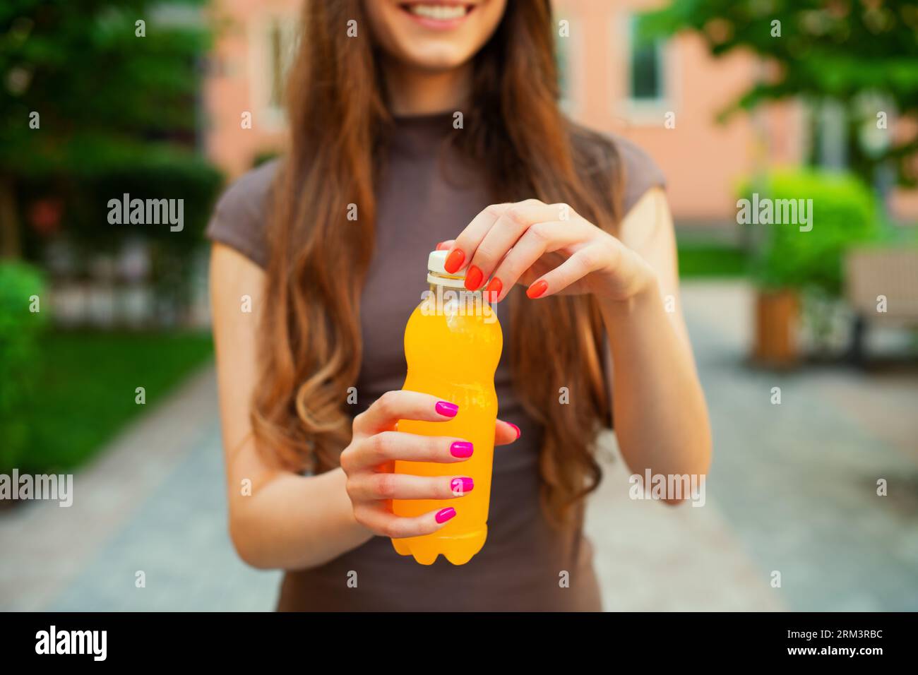 Unrecognizable young woman opens a Plastic Orange Lemonade Bottle on a ...