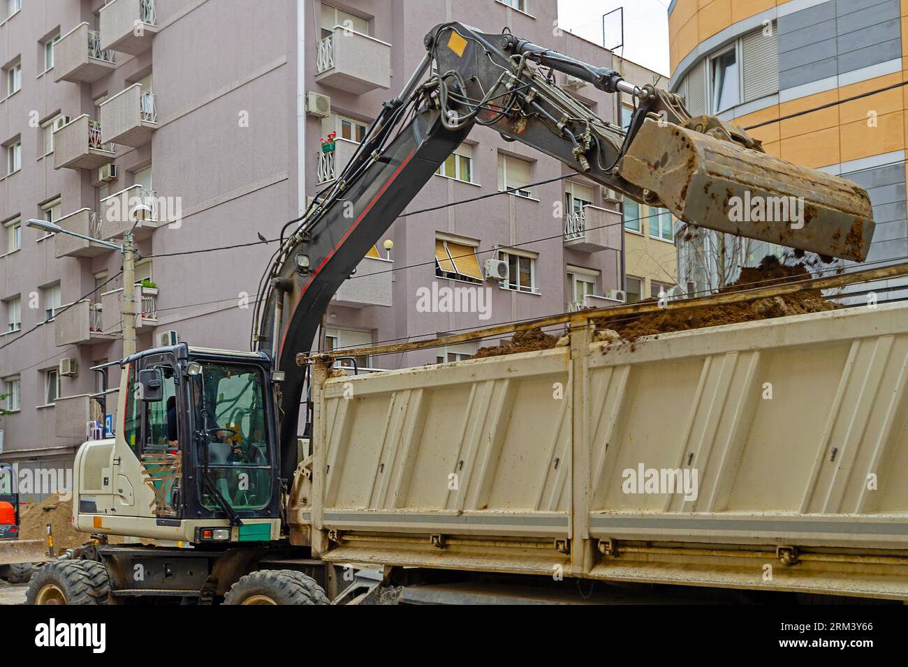 Excavator machine loading dirt in dumpster truck on construction site ...