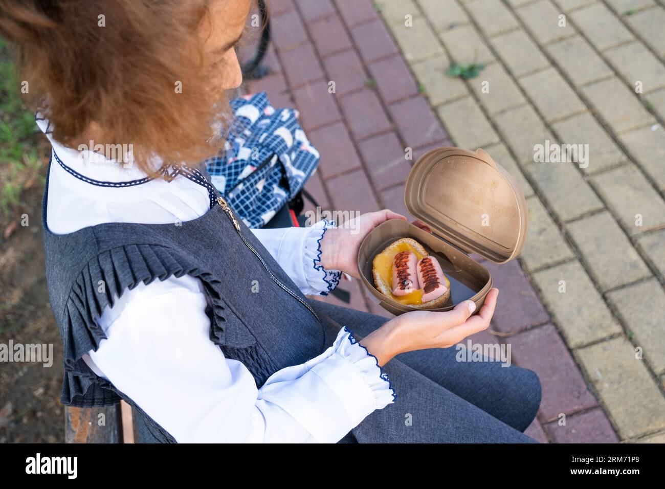 Girl with backpack eating sandwich packed in a sandwich box near school ...