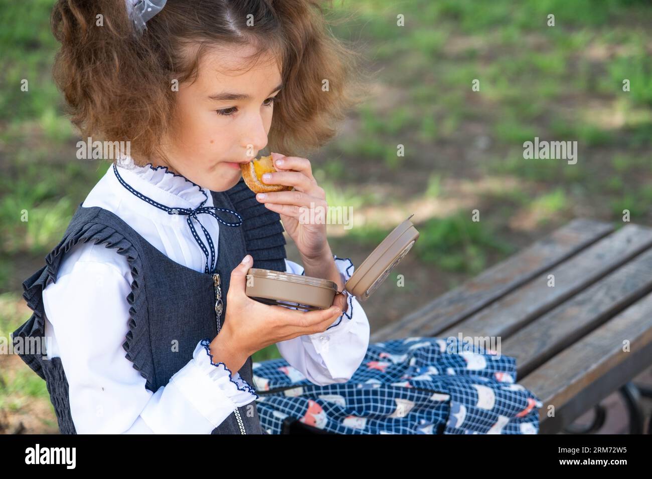 Girl with backpack eating sandwich packed in a sandwich box near school ...