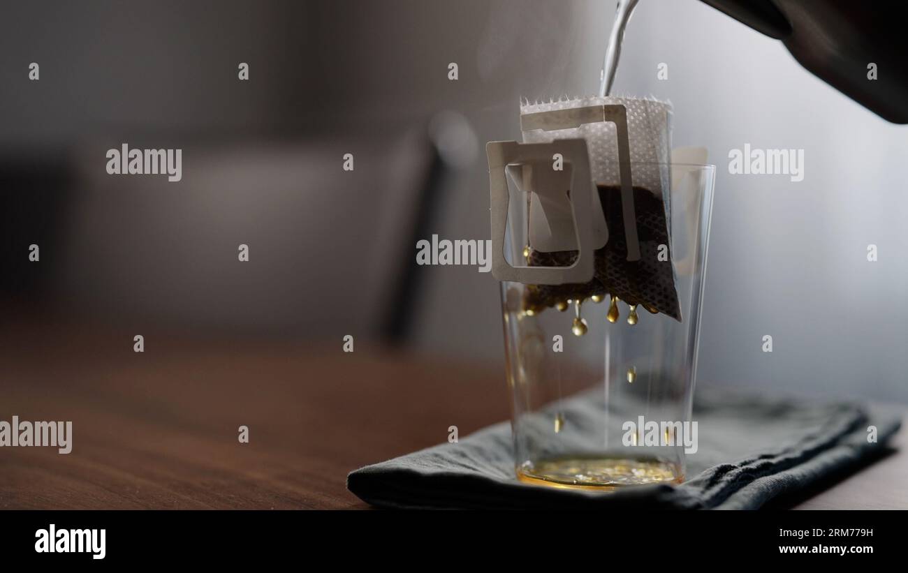 pouring hot water to make coffee with drip coffee bag on wood table ...