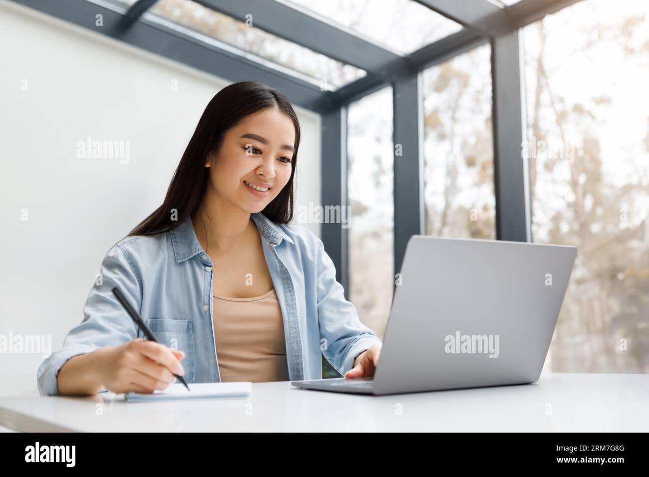Positive busy hardworking asian student lady writing notes, webinar ...