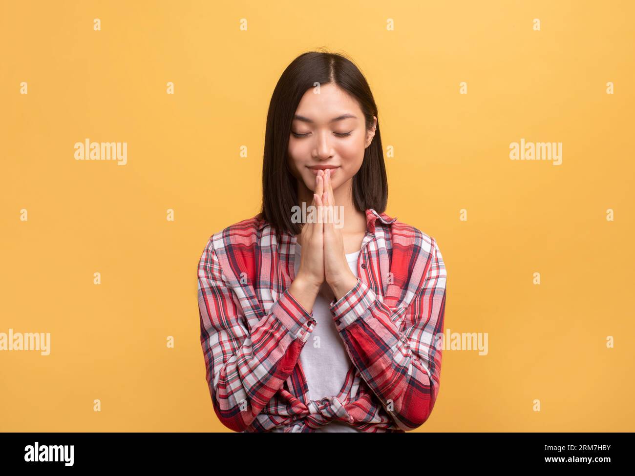 Portrait of glad young asian lady with closed eyes praying with clasped ...