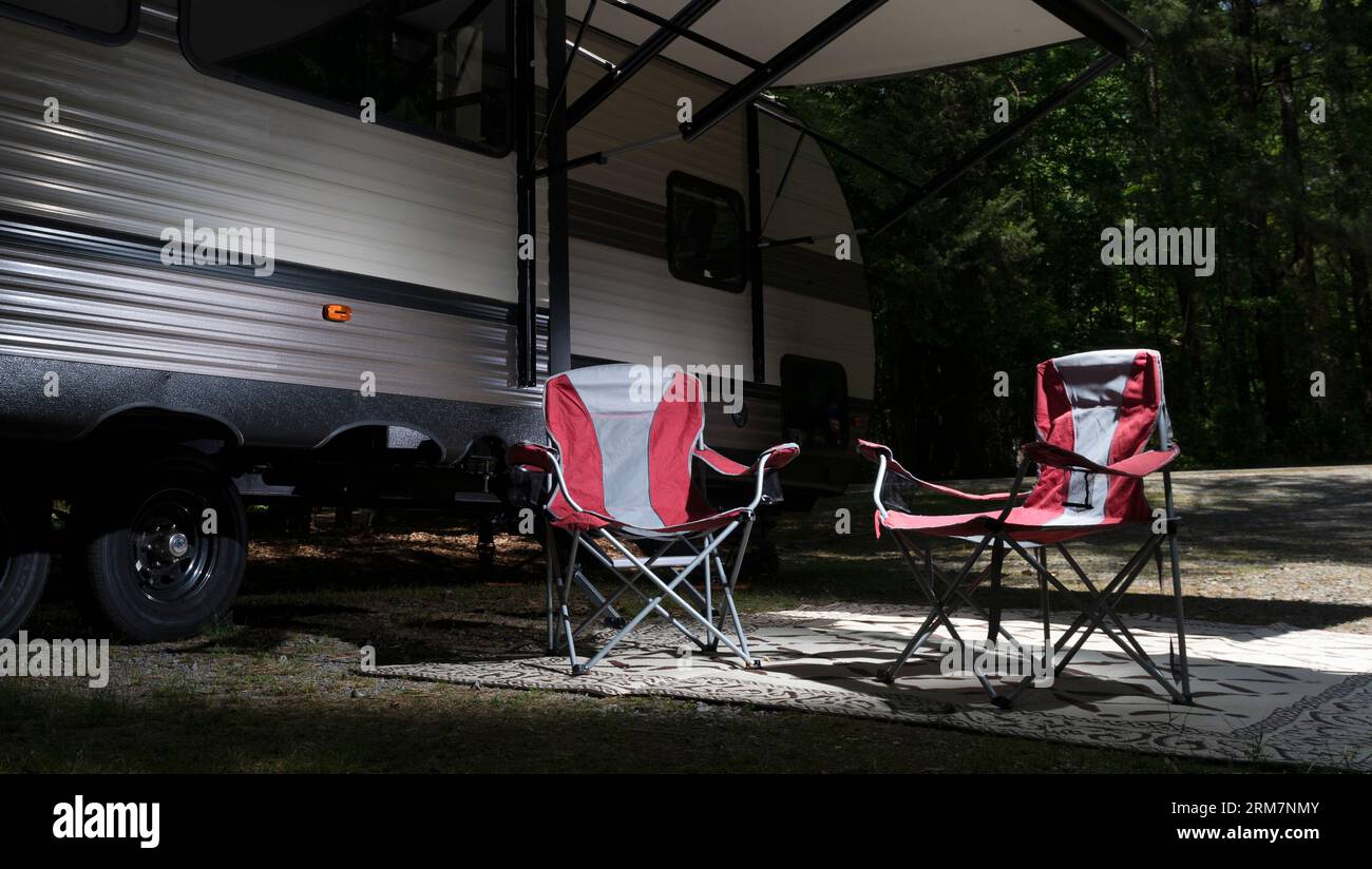 Camping chairs under the awning of a camping trailer with trees all ...
