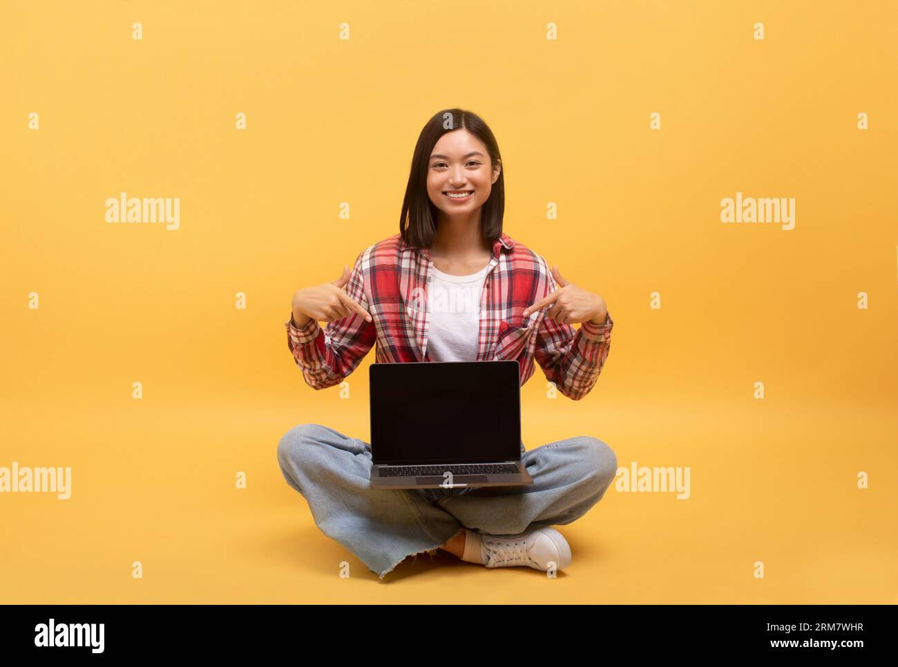 Happy asian lady in casual pointing fingers at laptop with black screen ...